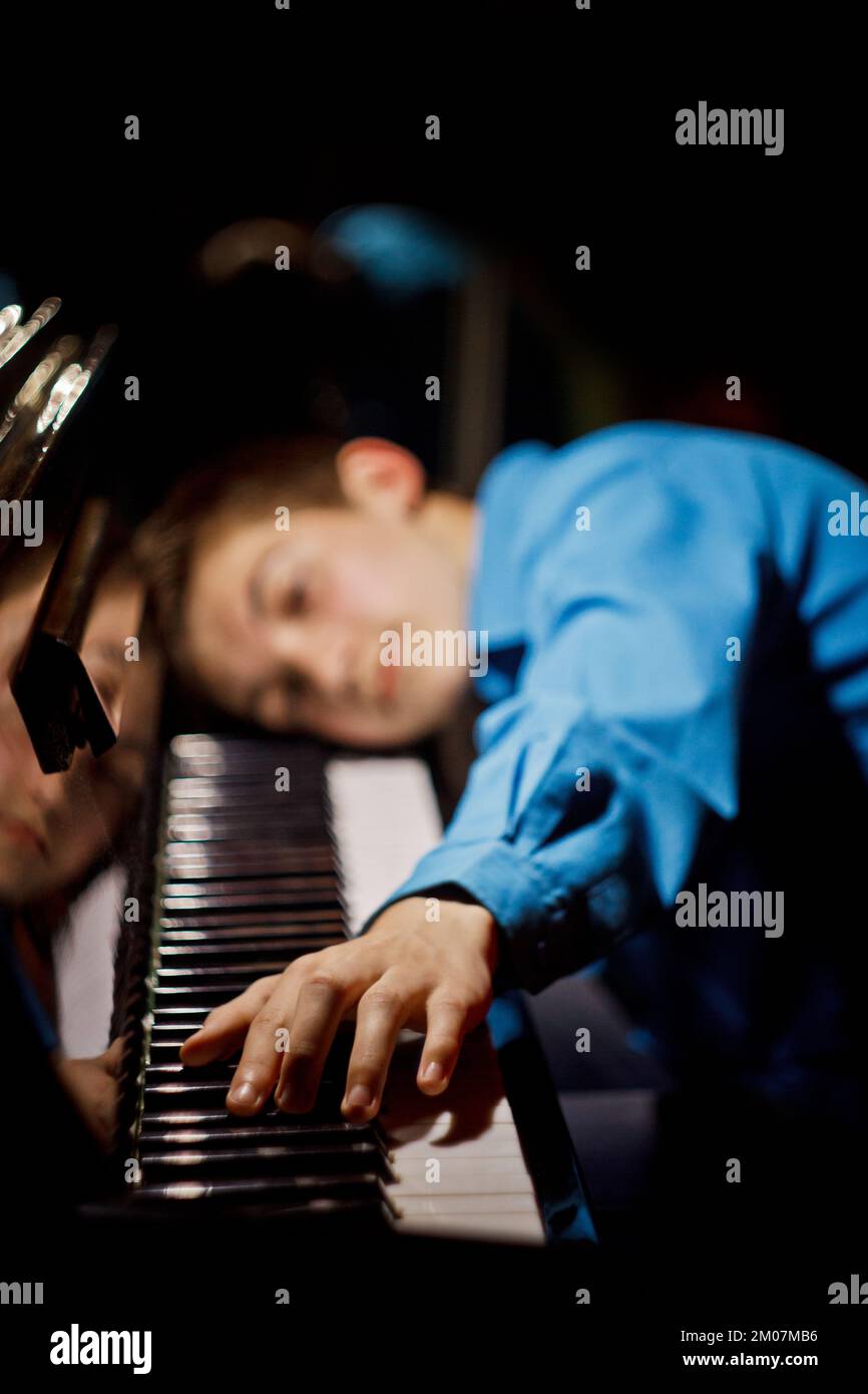 young man sitting at the piano. the boy lies on the keys and plays the ...