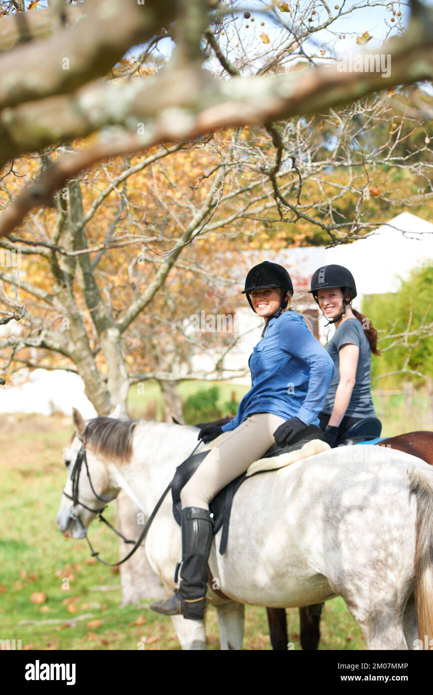 Looking back before riding out. Two young women on horseback smiling ...