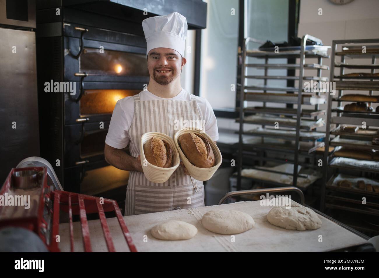 Young baker with down syndrome preparing pastries in bakery. Concept of ...