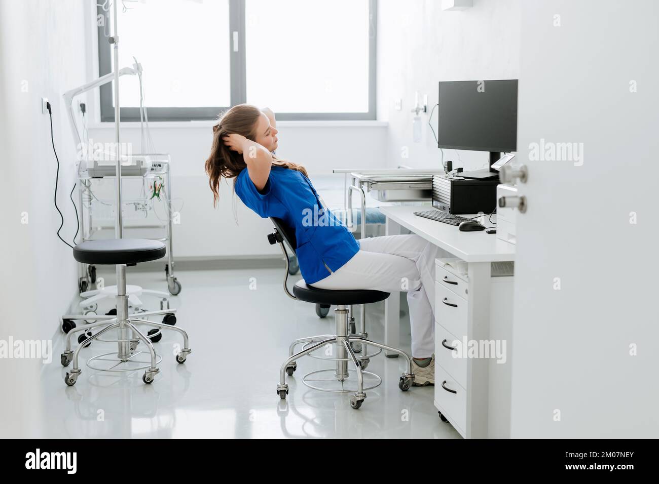 Young woman doctor stretching at hospital office desk Stock Photo - Alamy