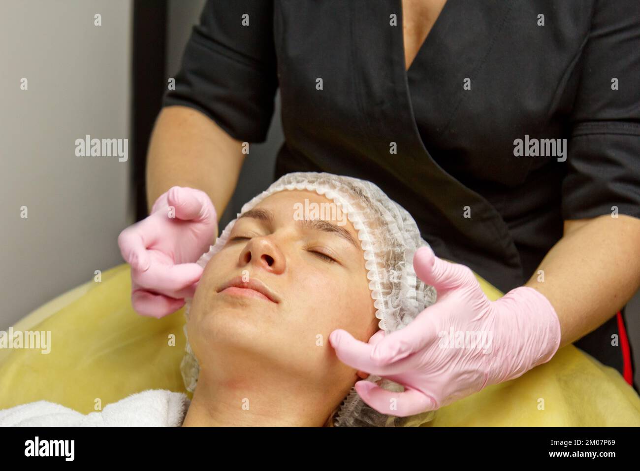 concept beautician. The hands of a cosmetologist put cream on the face ...