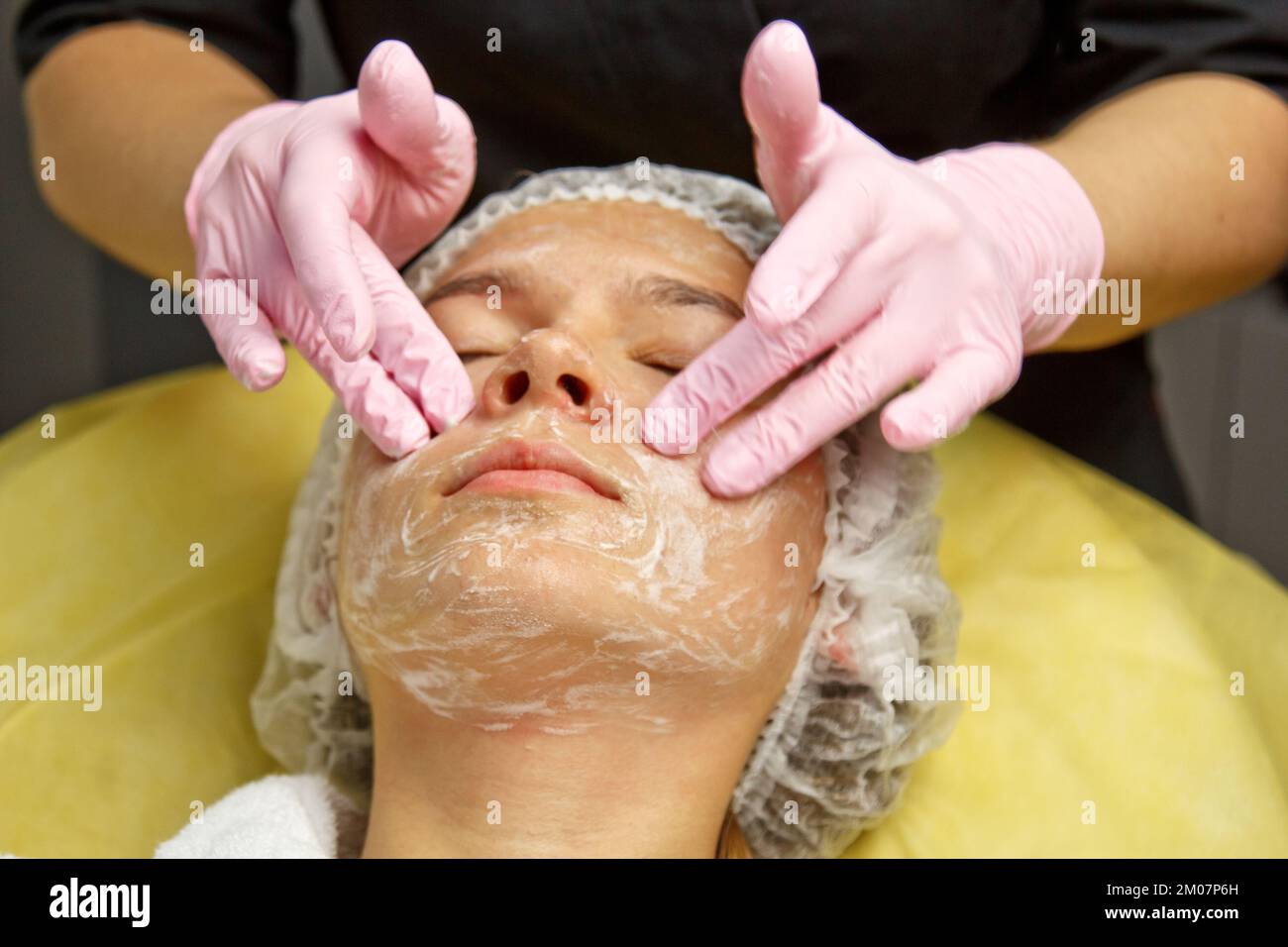 concept beautician. The hands of a cosmetologist put cream on the face ...