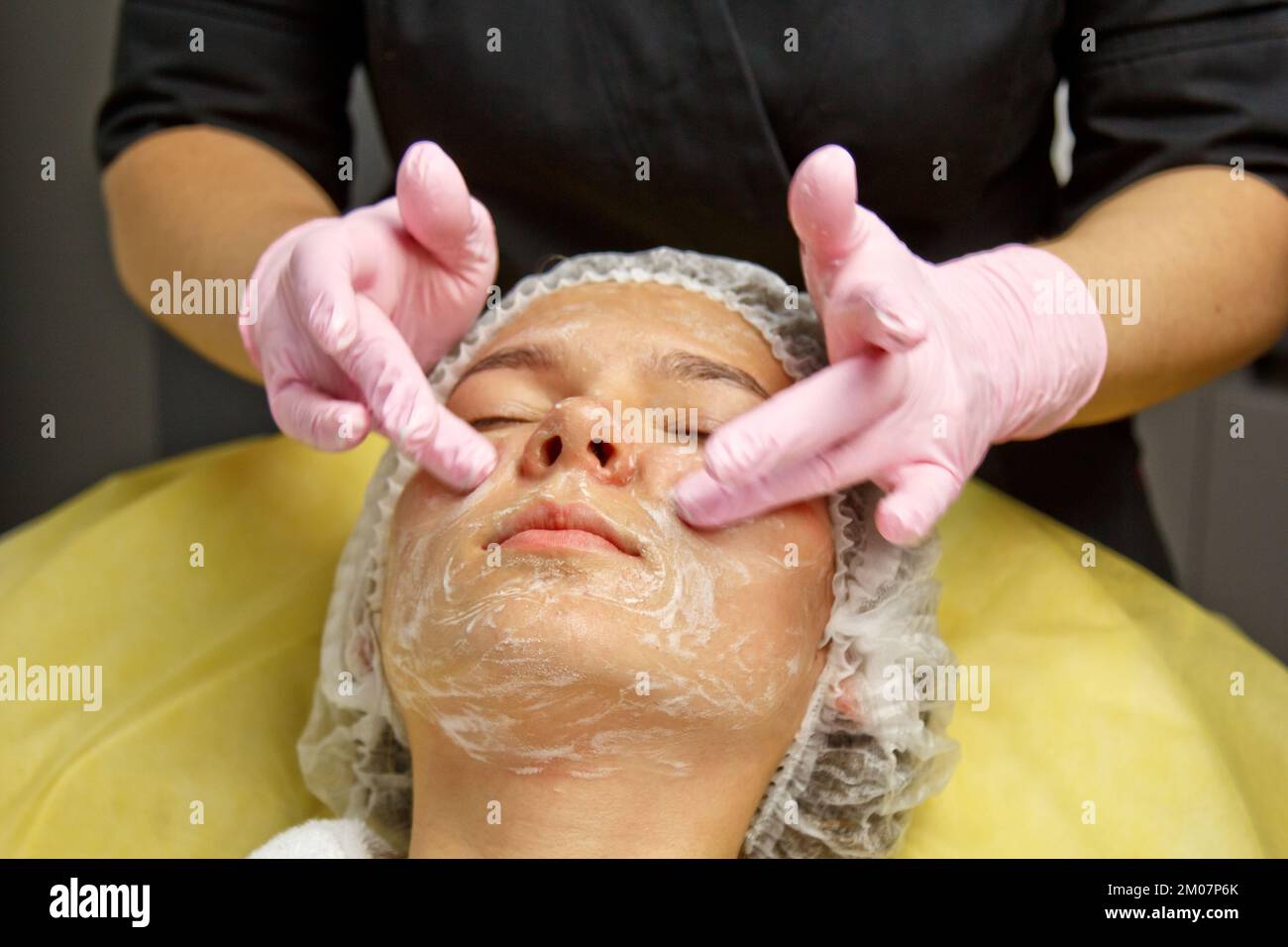 concept beautician. The hands of a cosmetologist put cream on the face ...