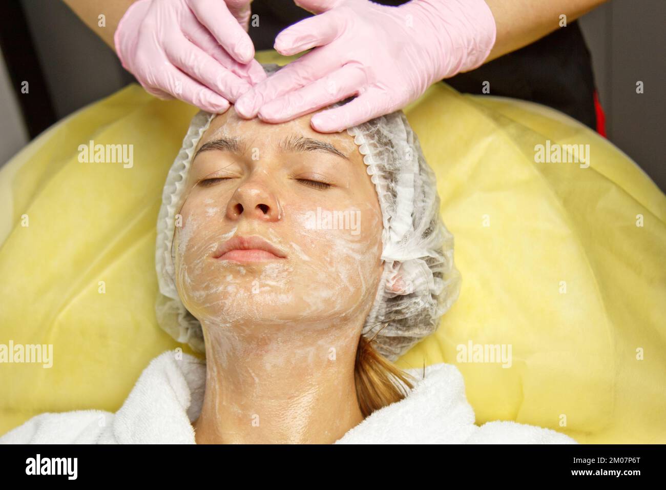 concept beautician. The hands of a cosmetologist put cream on the face ...