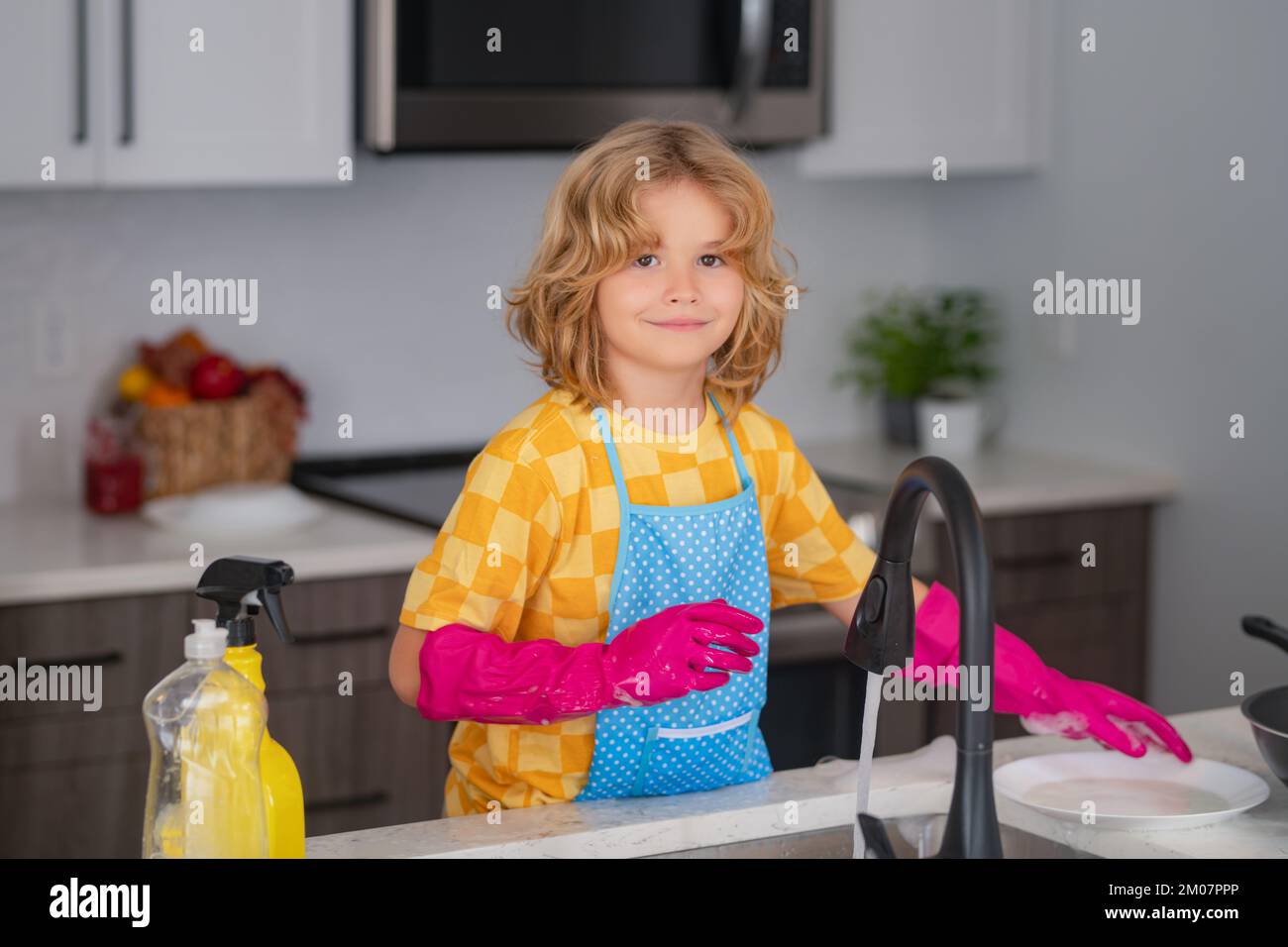 Child doing and wiping dishes in kitchen. Little kid cleaning at home ...