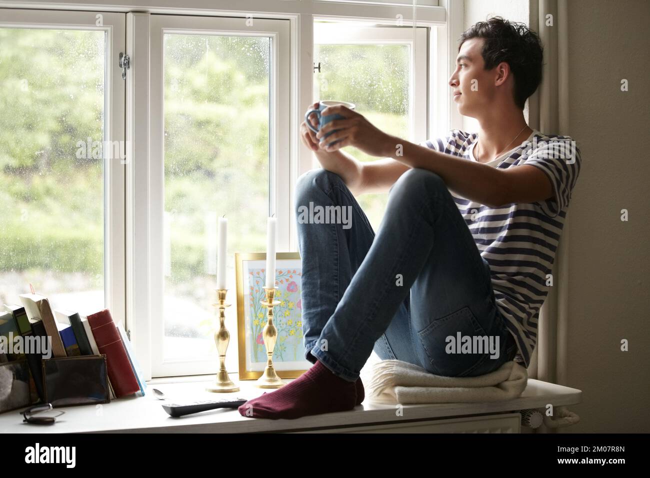 A moments reflection. Casual young guy sitting indoors and drinking a ...