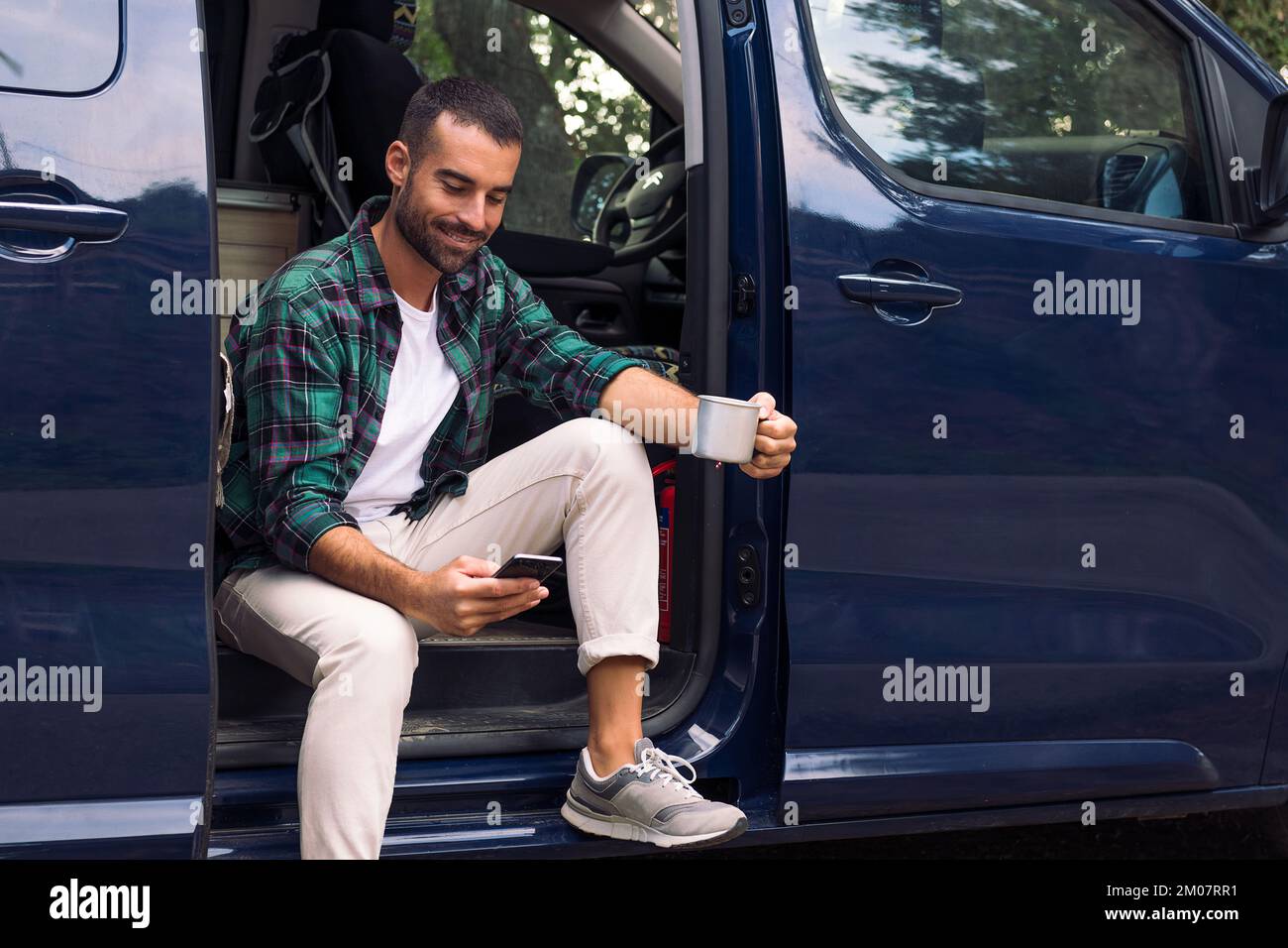 man using phone sitting in the door of his camper Stock Photo - Alamy