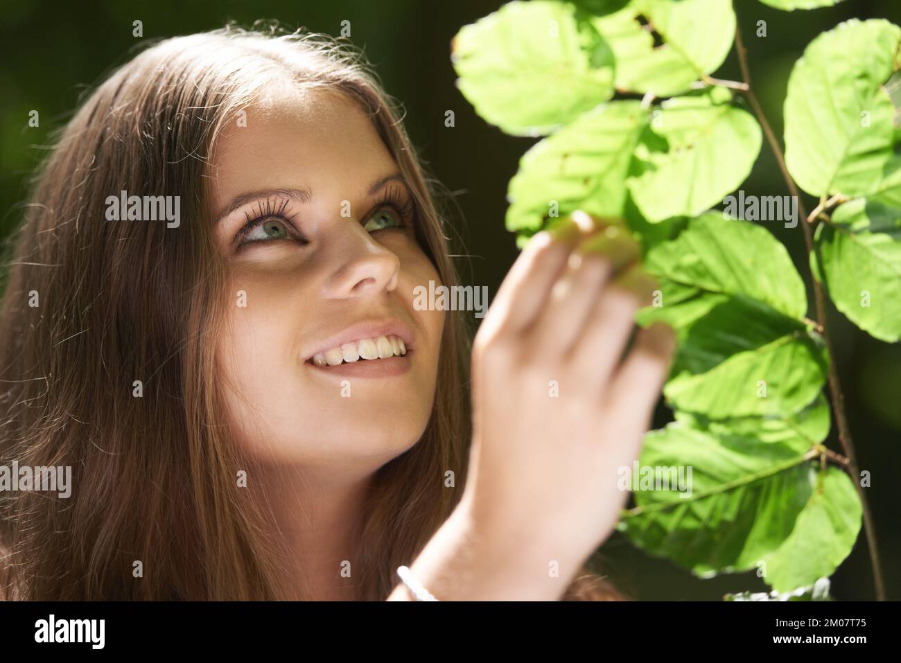 Feeling close to nature. A pretty young woman looking at the leaves on ...