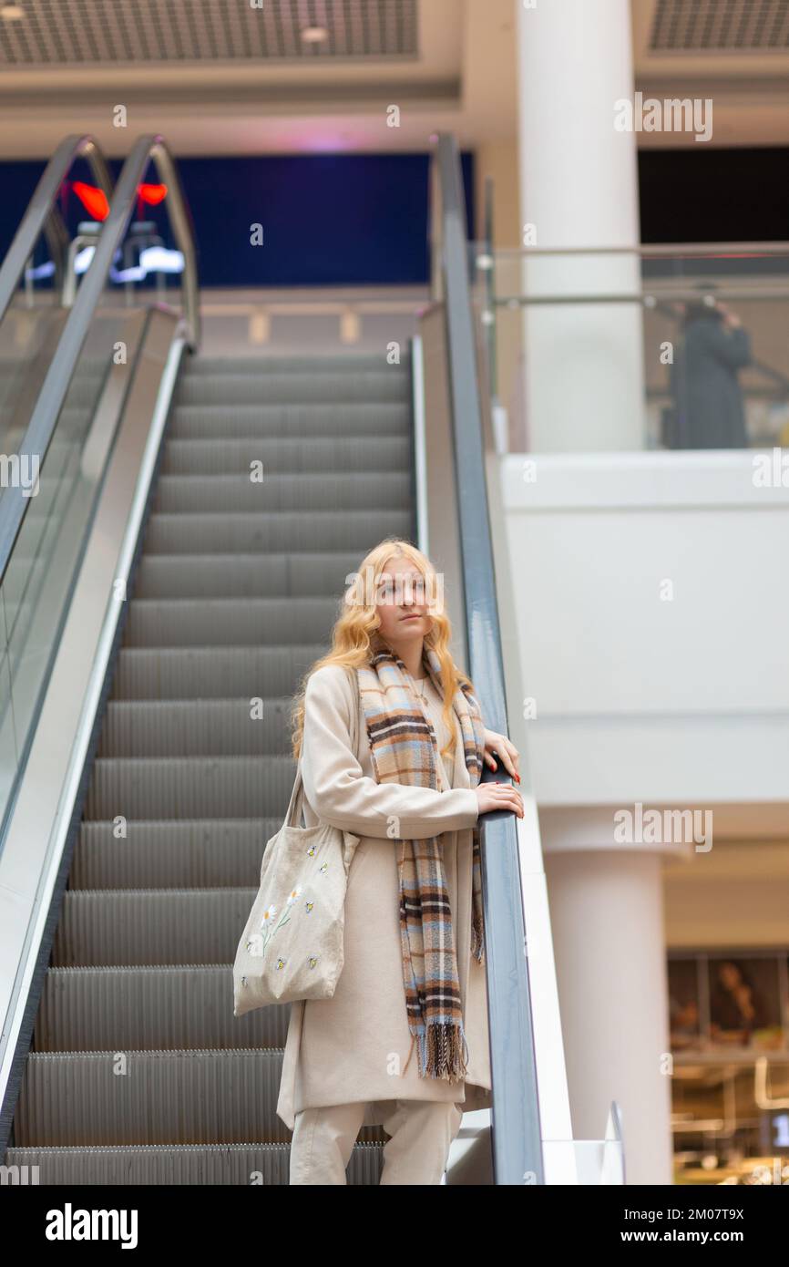 Young woman with long blond hair moving up on escalator at shopping ...