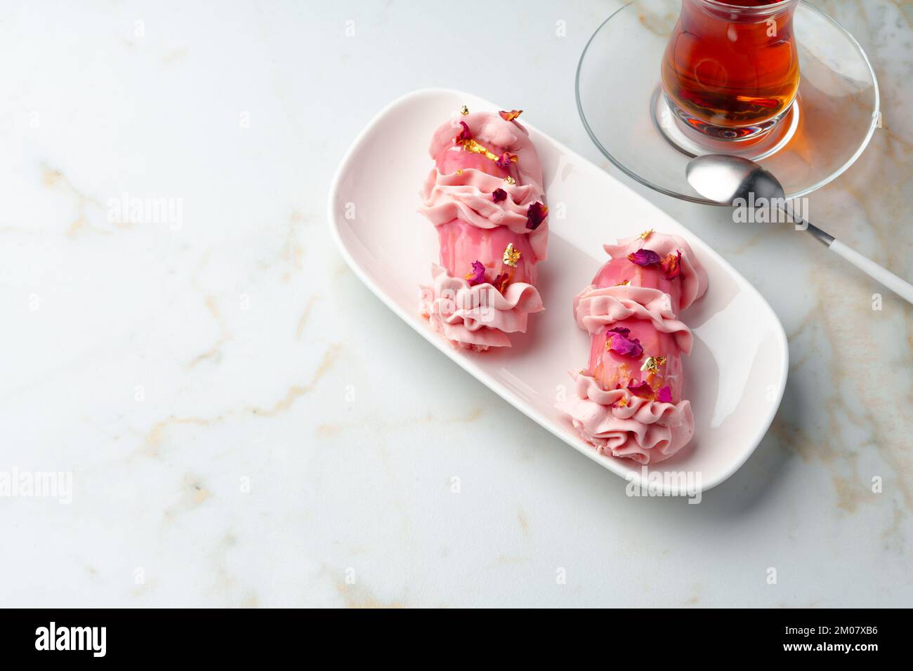 Eclair dessert with pink icing on white table Stock Photo - Alamy