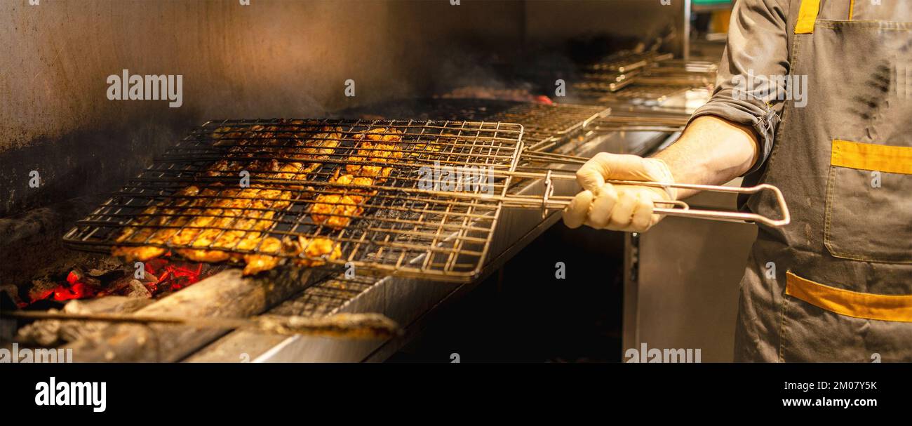 A high-angle of a hand grilling meat on grill mesh coal and smoke ...