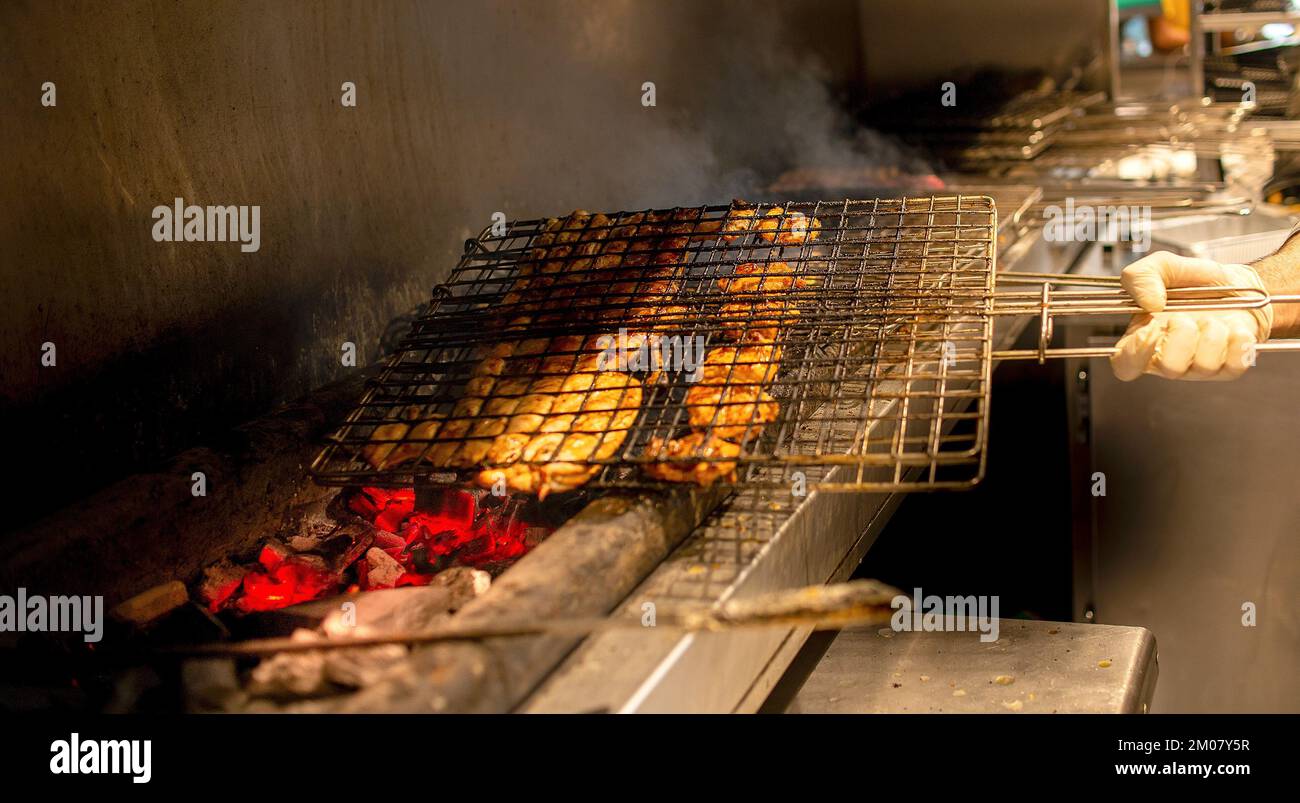 A high-angle of a hand grilling meat on grill mesh coal and smoke ...