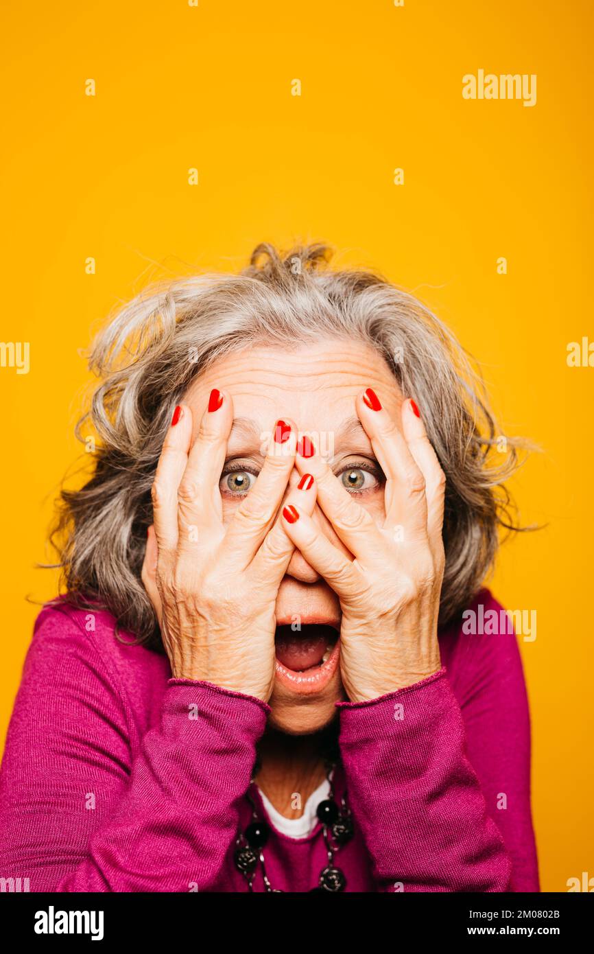 Portrait of a senior woman covering her face with her hands over a ...