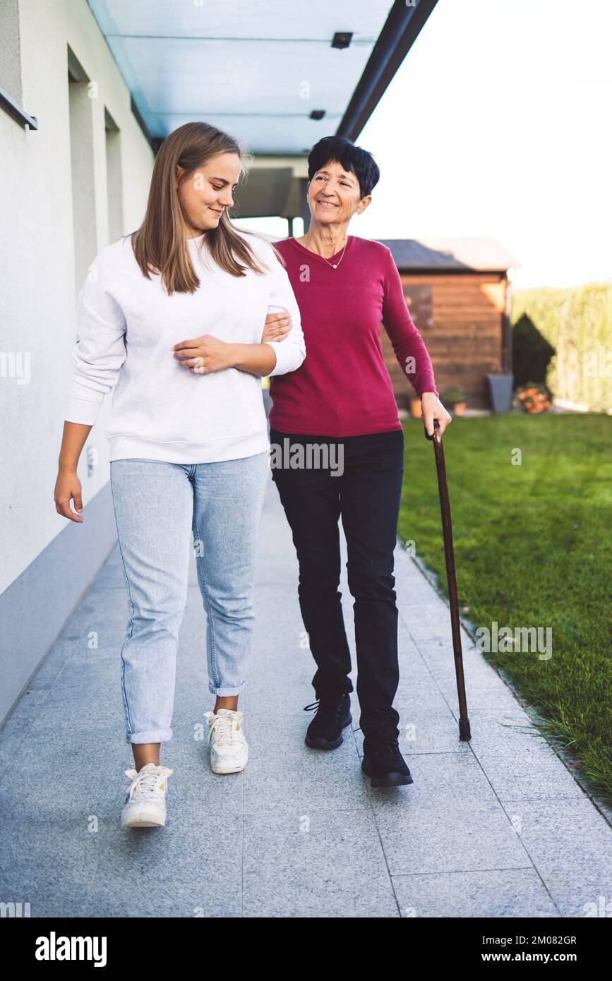 Senior woman walking with a cane in one arm and holding for nurses hand ...