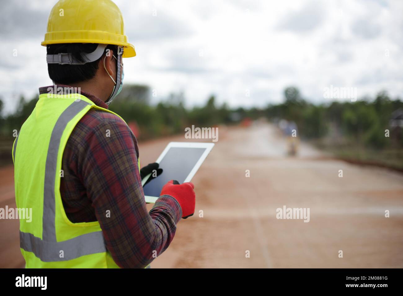 A male contractor wearing a helmet with a tablet stands inspecting work at a rural concrete road ...