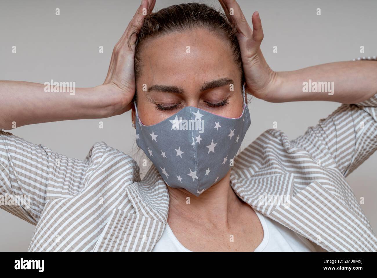 A woman wearing a medical mask on her face holds her hands near her ...