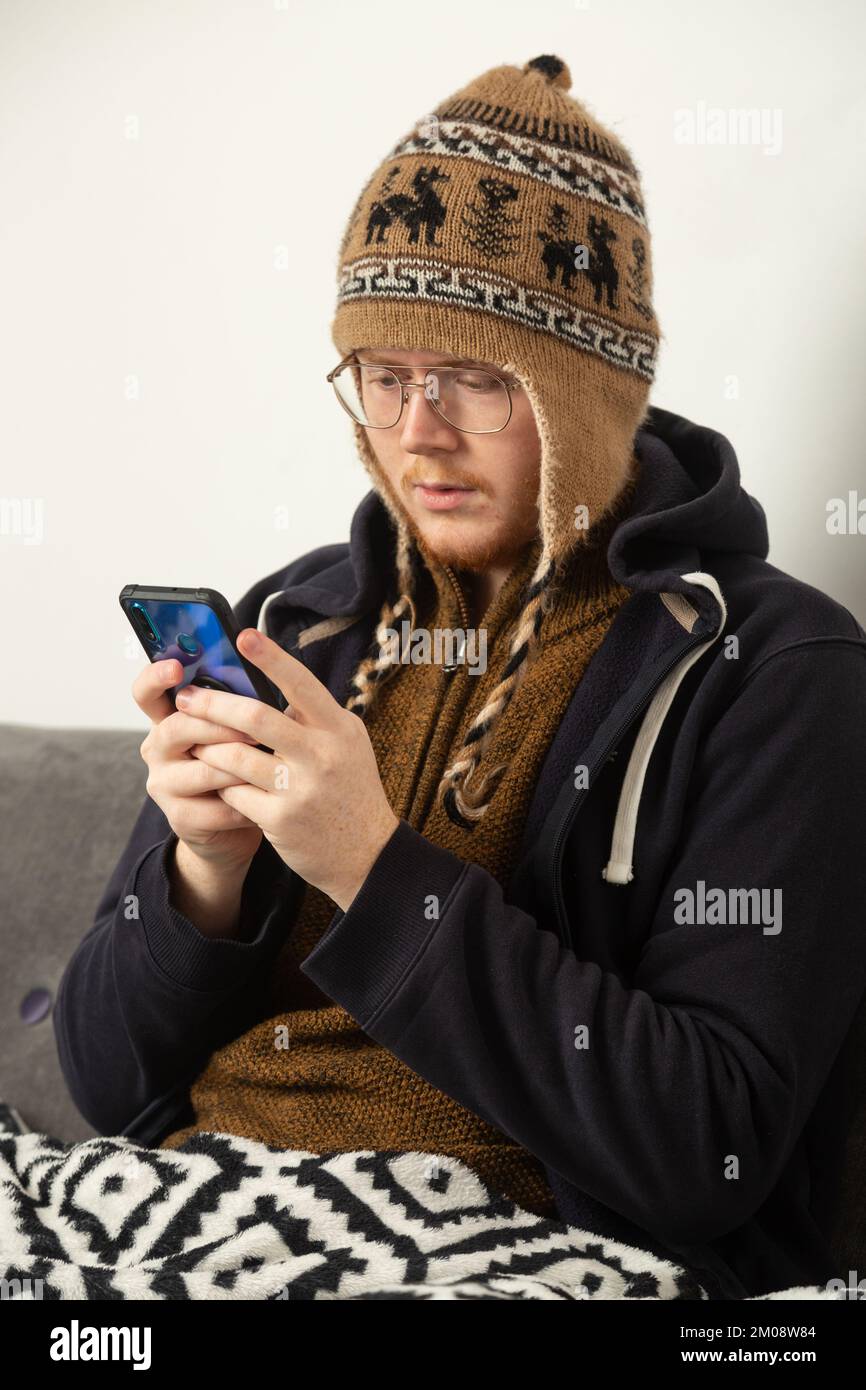 A young man wearing winter clothing and a blanket while using his ...