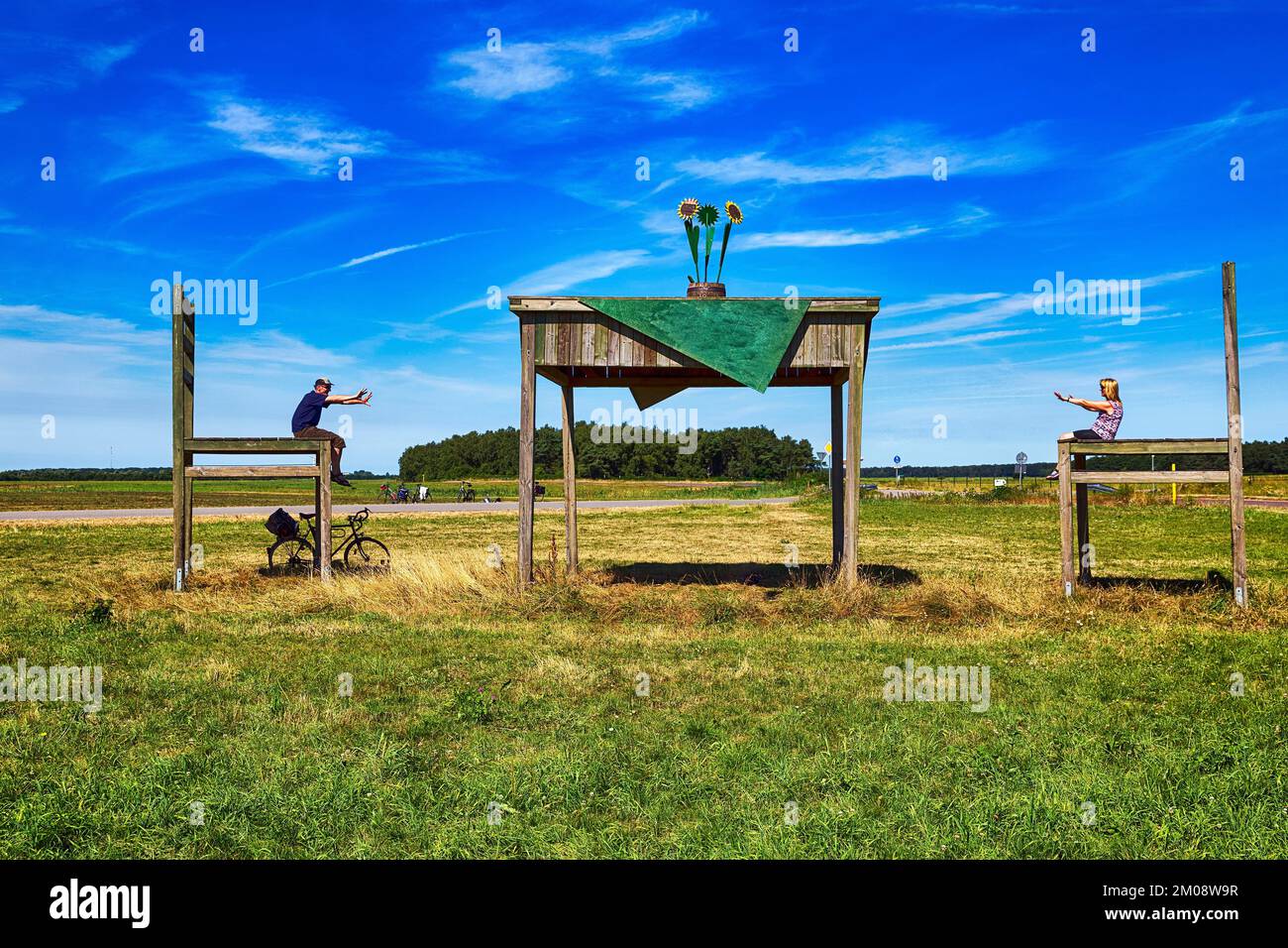 Oversized table with two chairs on a meadow, passers-by taking a break ...
