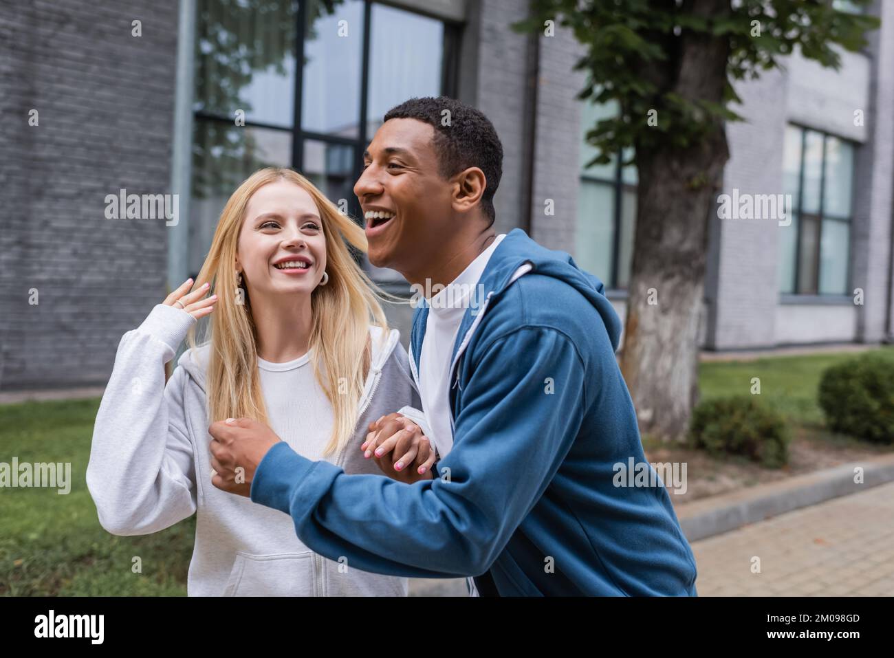 happy blonde woman looking at african american boyfriend laughing on ...