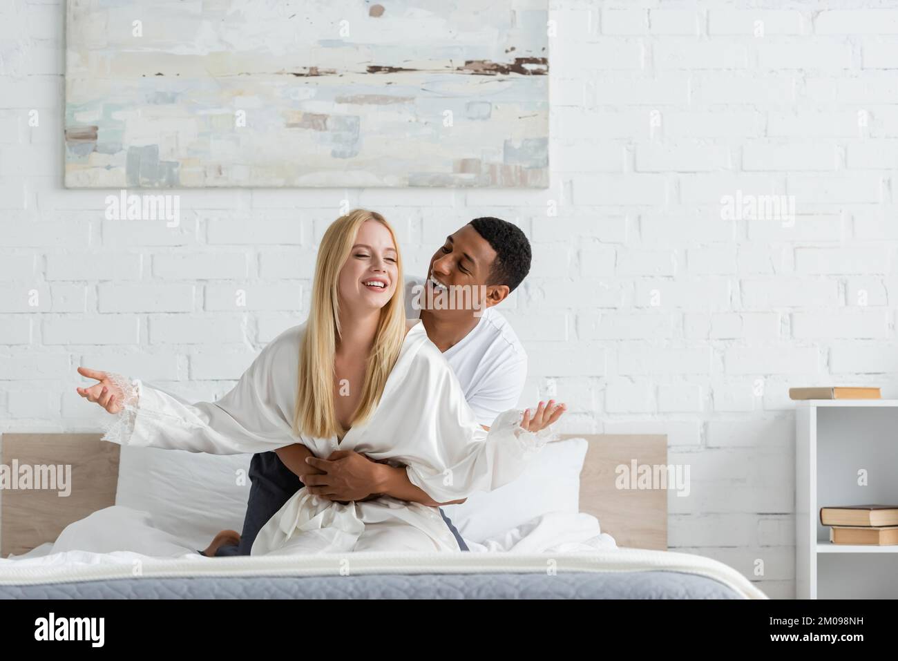 happy african american man hugging waist of woman in white robe sitting ...