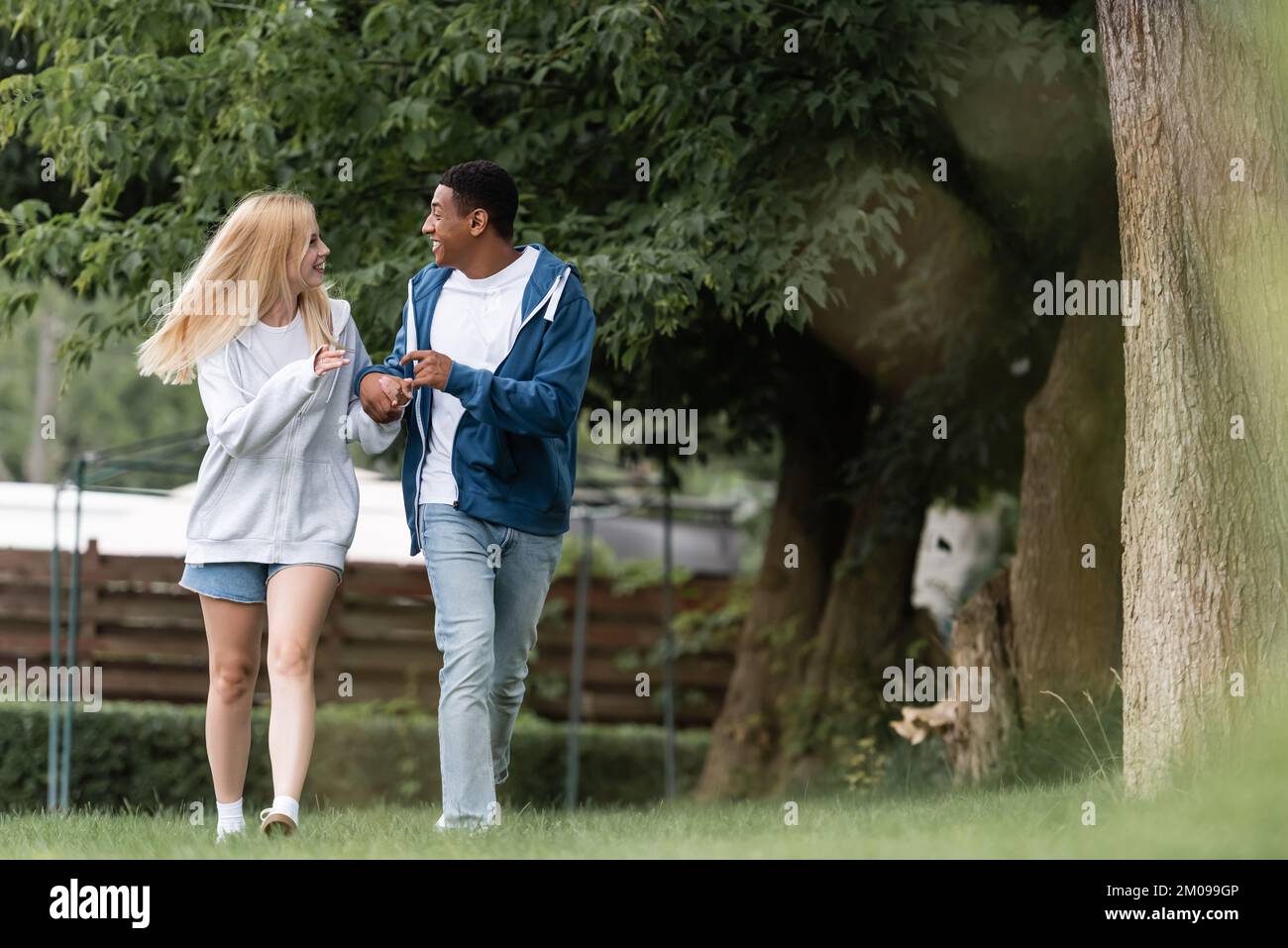 full length of happy multiethnic couple walking and talking in park ...