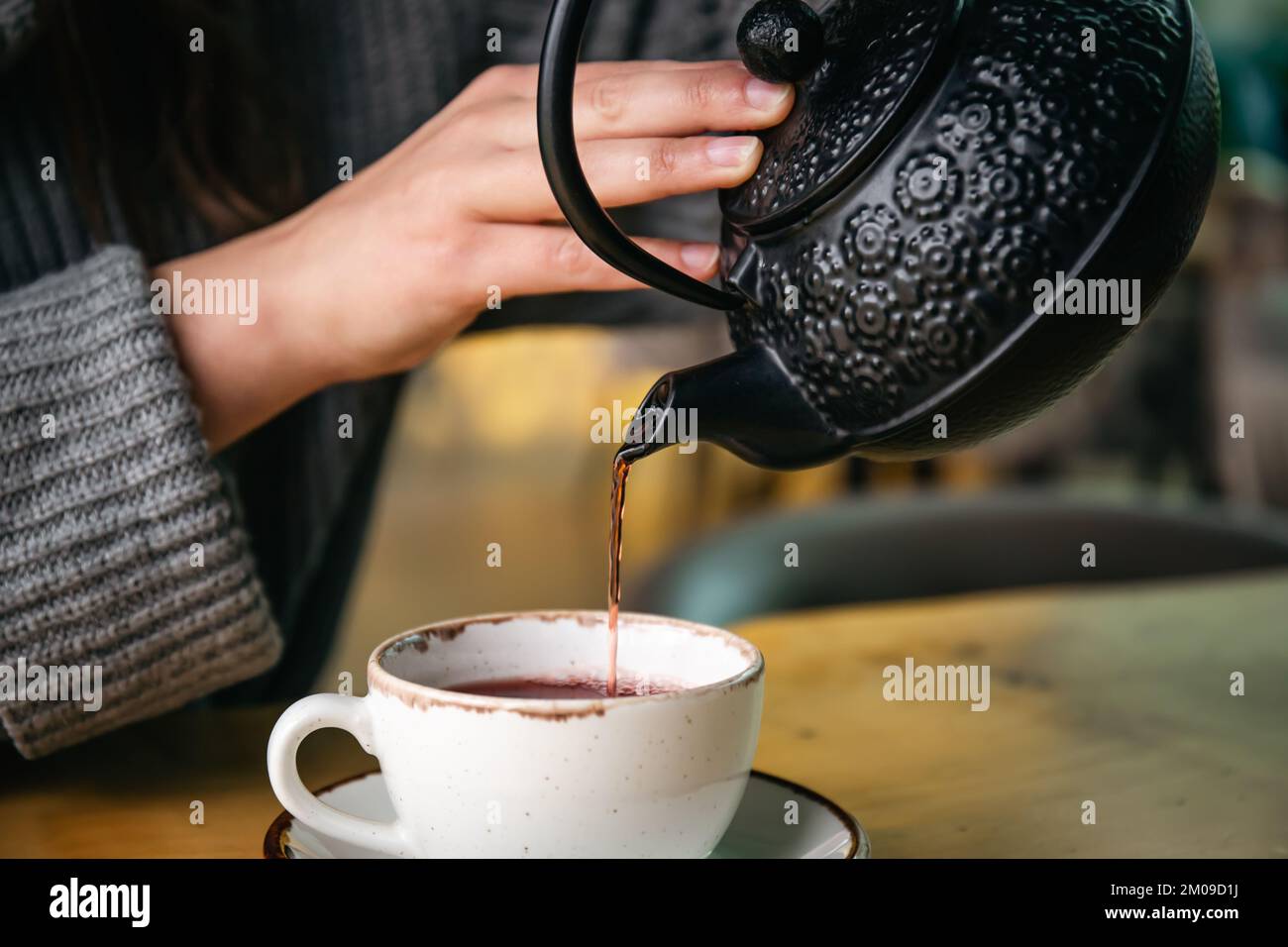 Woman in a cafe pour tea from a black cast iron teapot Stock Photo - Alamy