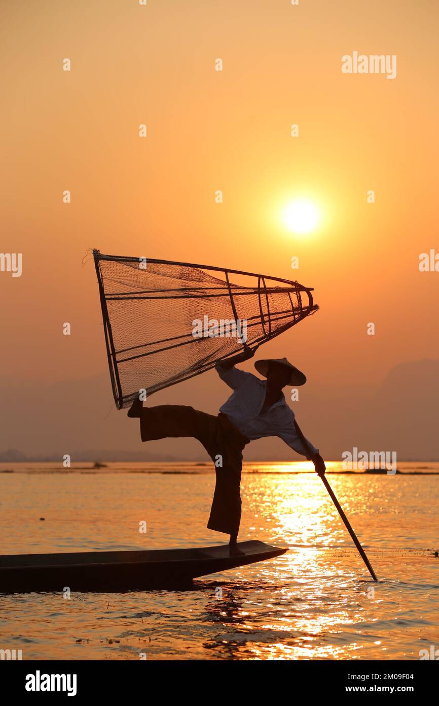 A silhouette of a fisherman near a lake catching fish in a traditional ...