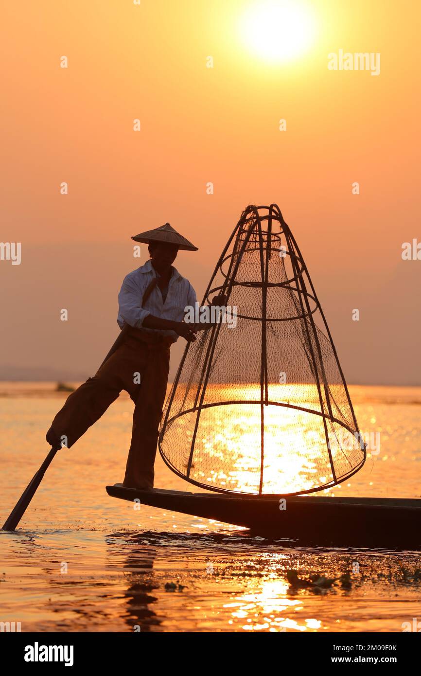 A silhouette of a fisherman near lake catching fish in a traditional ...