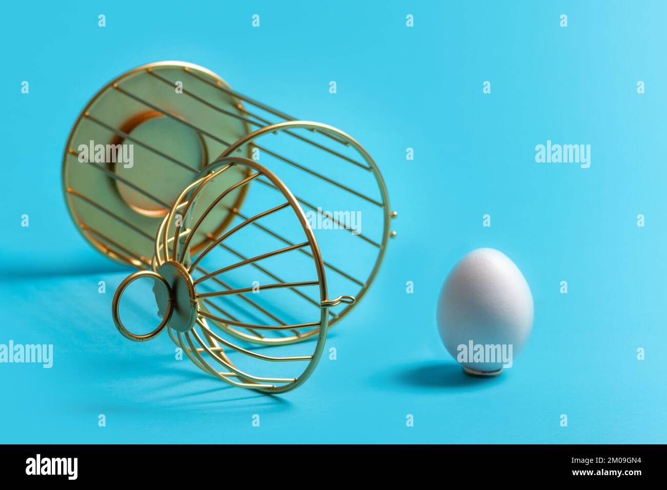 Upside down open cage with an egg outside on a blue background. The ...