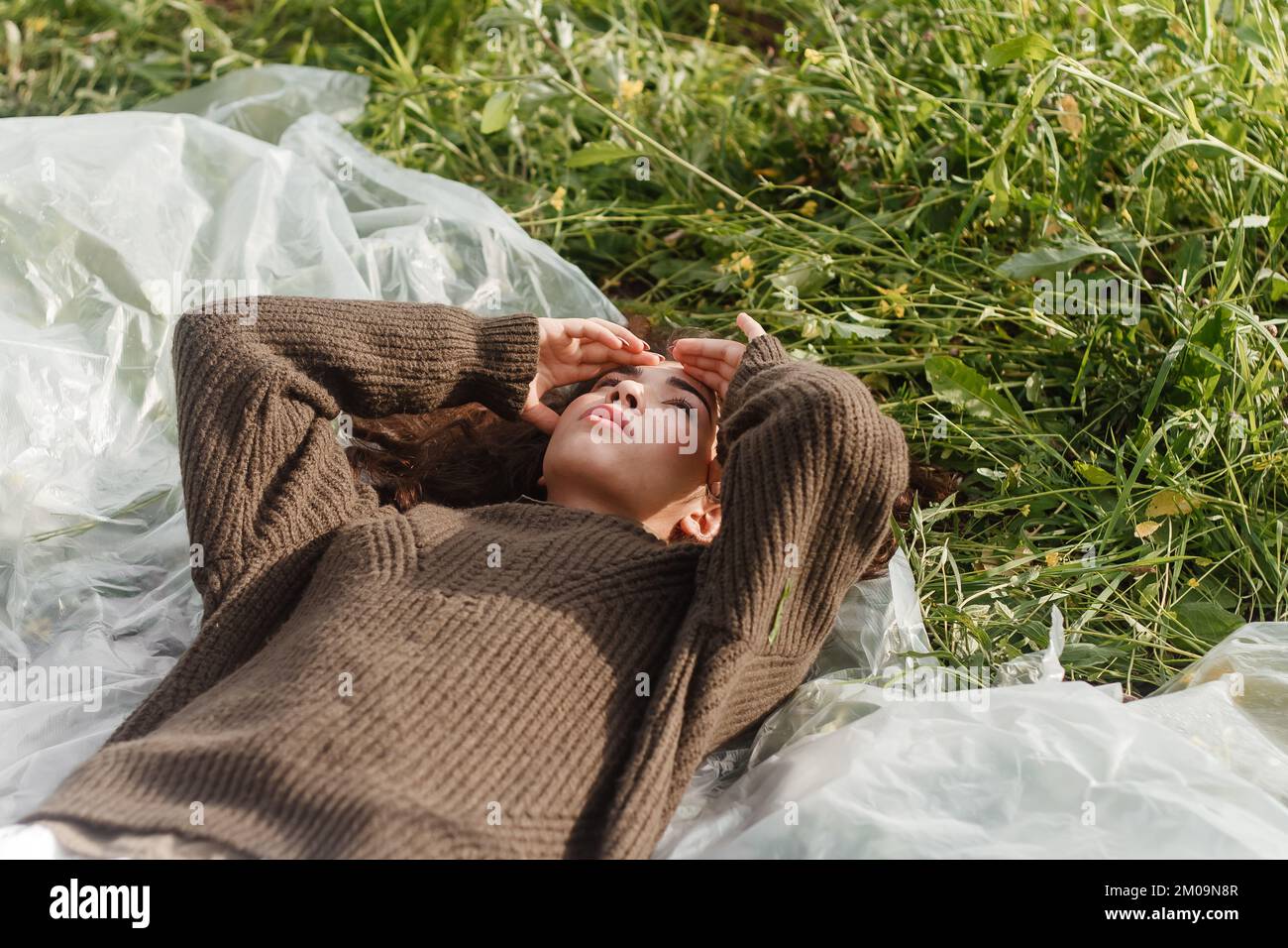 An Asian woman is lying on the ground in a field in a brown sweater ...