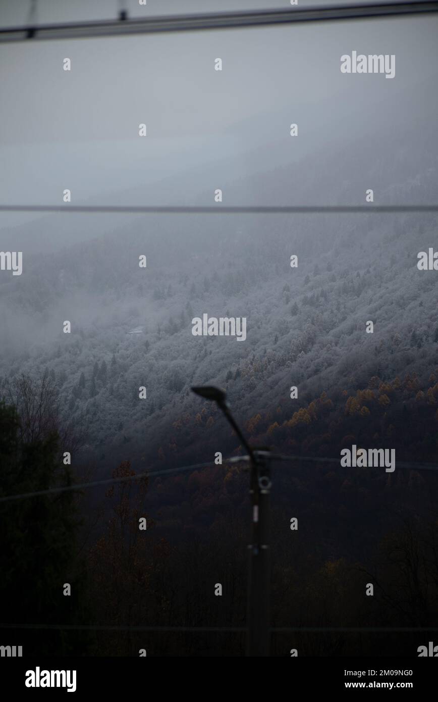 A vertical shot of a street lamp in front of a mountain slope covered ...