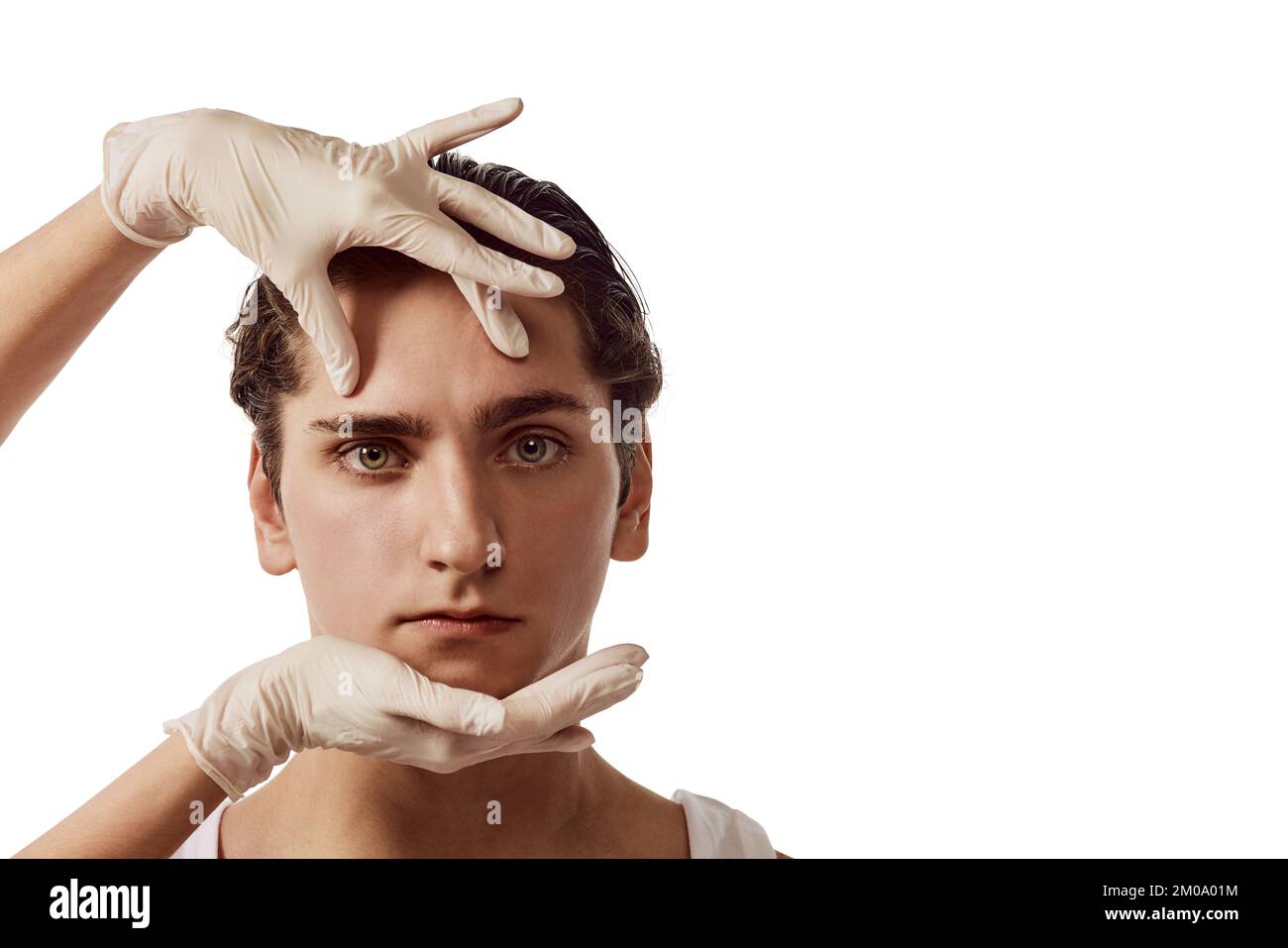 Portrait of young man and female hands in gloves on male face isolated over white background ...