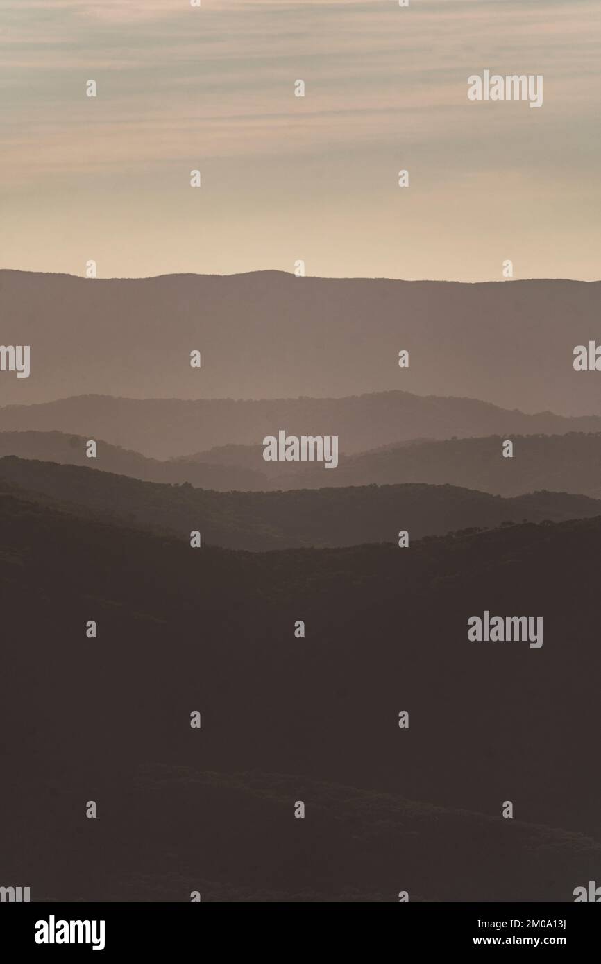 A vertical aerial view of beautiful mountain silhouettes under a bright ...