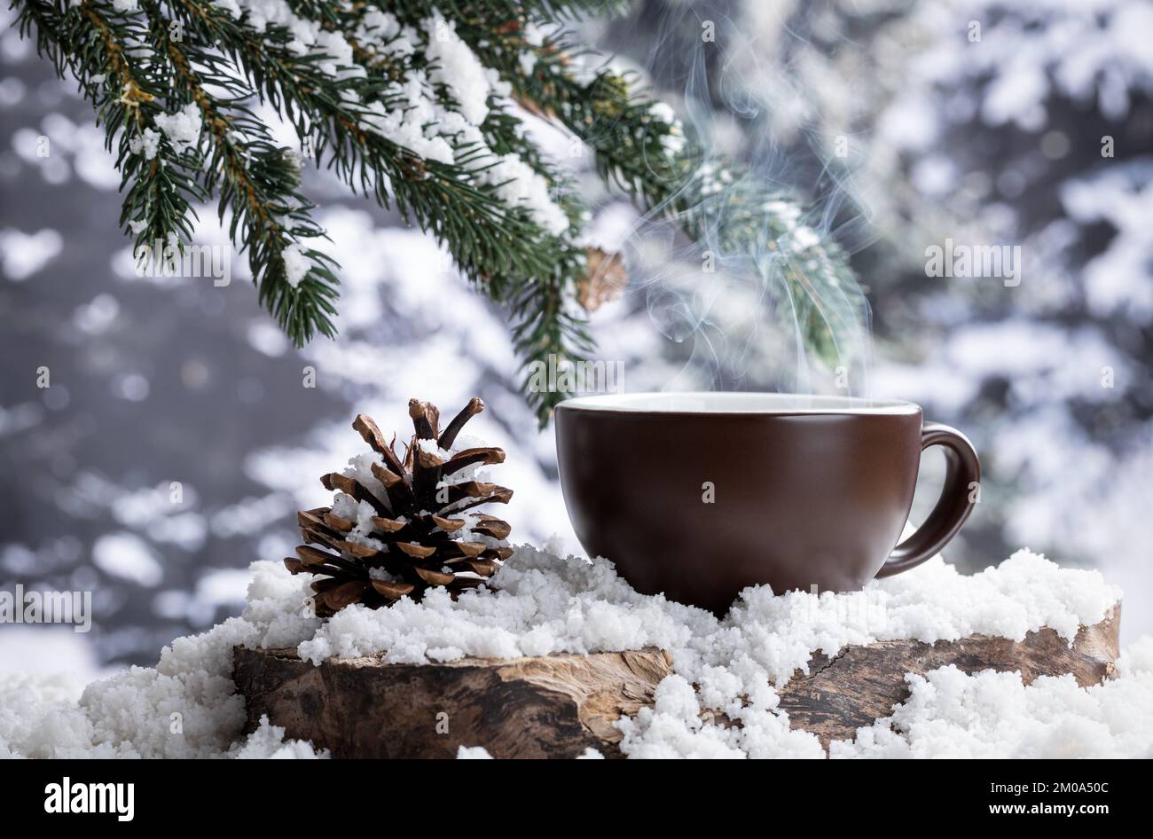 Steming hot drink in a coffee cup outdoors on a tree stump with a snowy ...