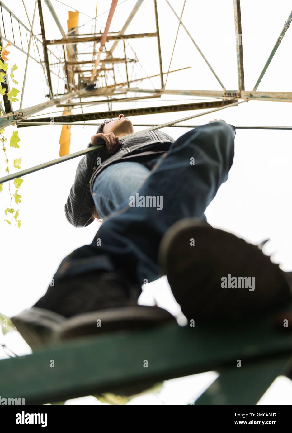 Young girl climb on a windmill dressed in leather jacket and blue jeans ...