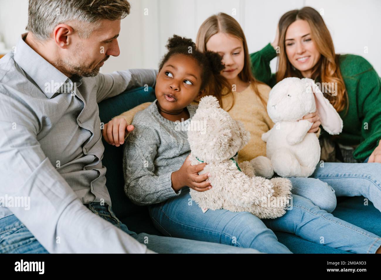 Happy family with adopted african little girl sitting on couch in ...