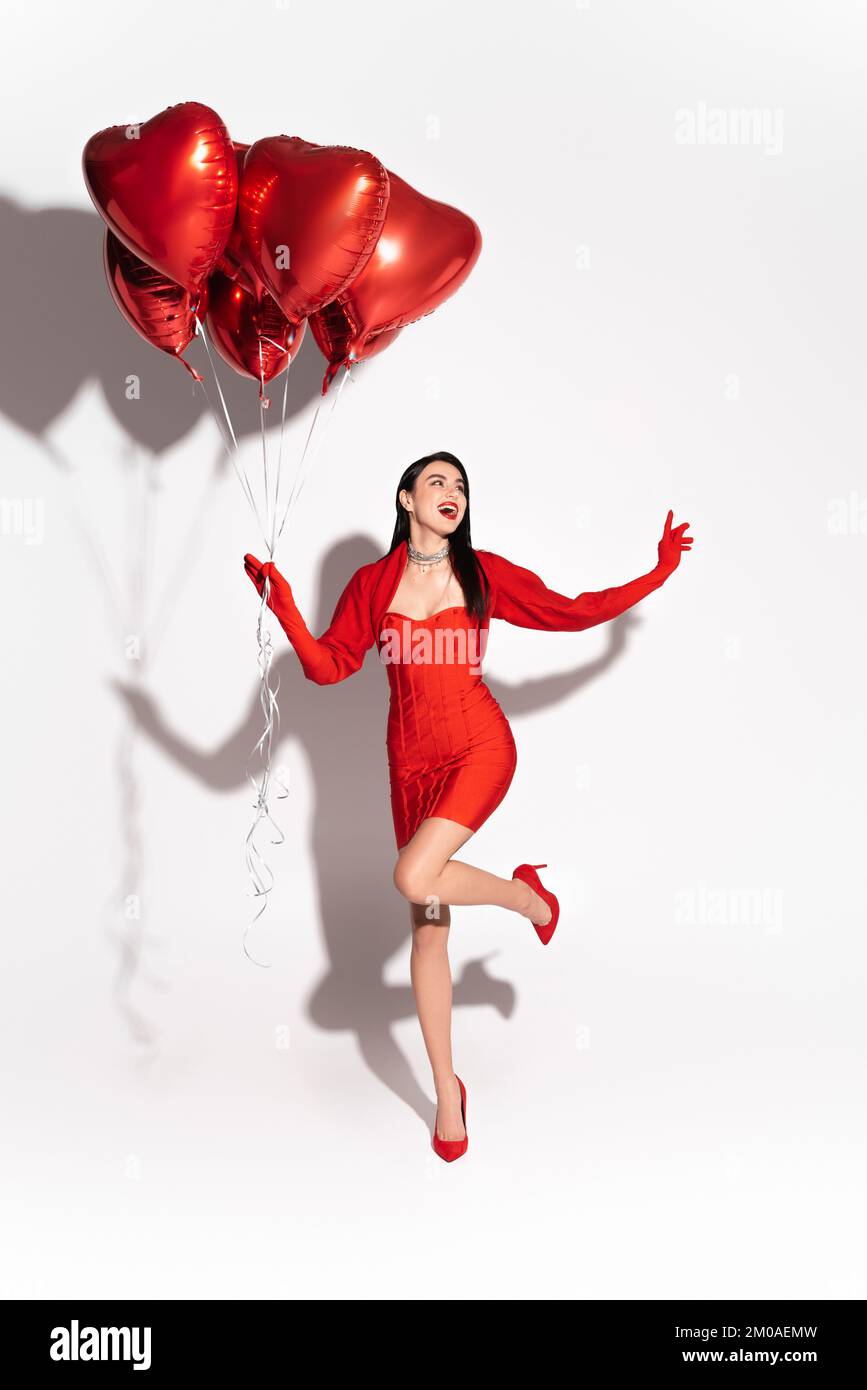 Excited woman in dress and heels holding red heart shaped balloons on ...