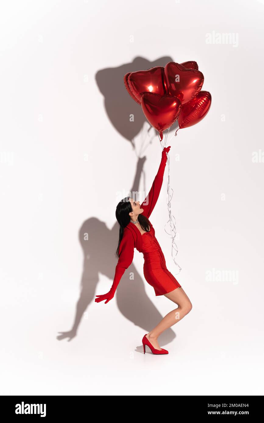 Side view of stylish woman in dress and heels pulling heart shaped ...