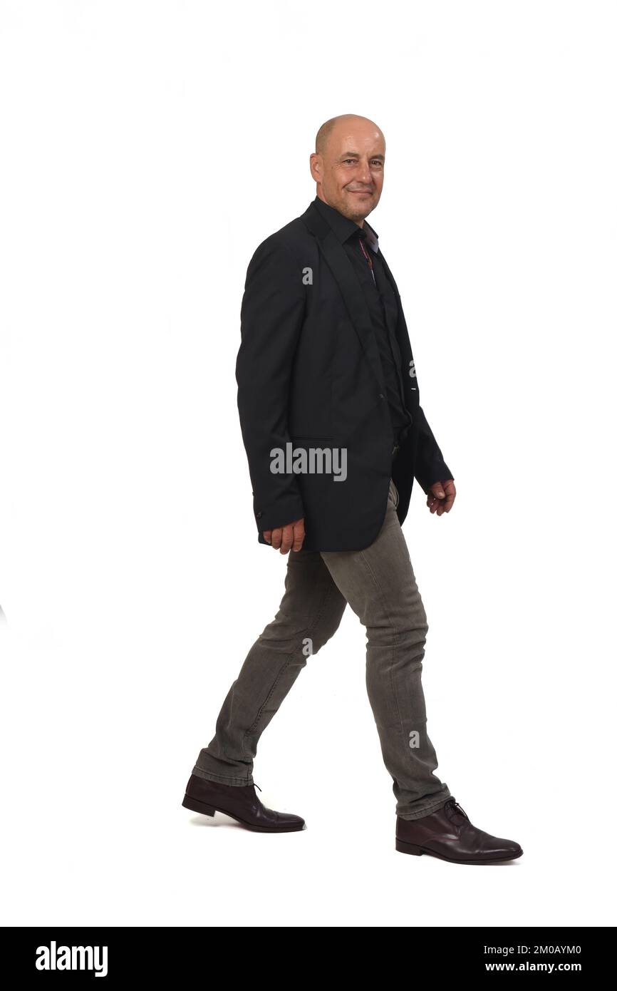 side view of a man with blazer and jeans walking and looking at camera ...