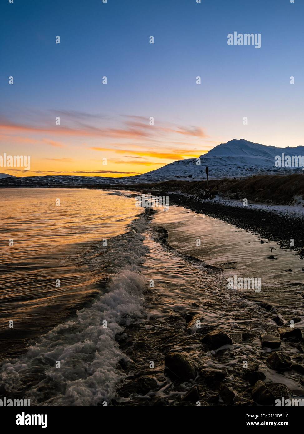 A picturesque scene with vibrant sunset sky over the wavy sea and snow ...