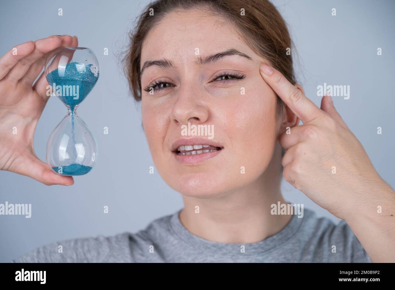 Caucasian red-haired woman holds an hourglass and examines the wrinkles ...
