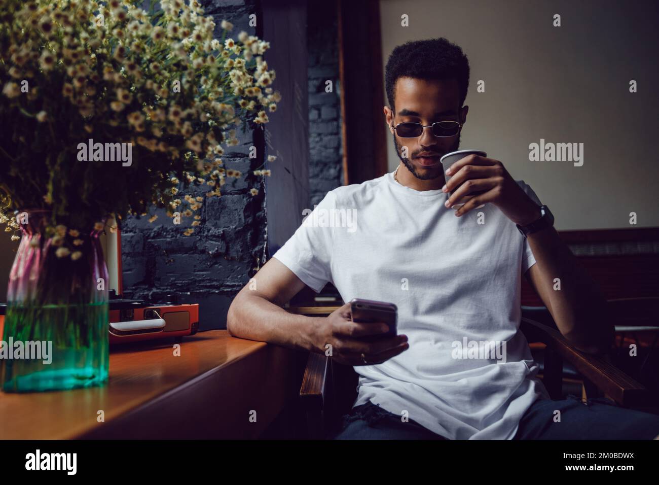African american man in a white t-shirt sits in a coffee shop and uses ...