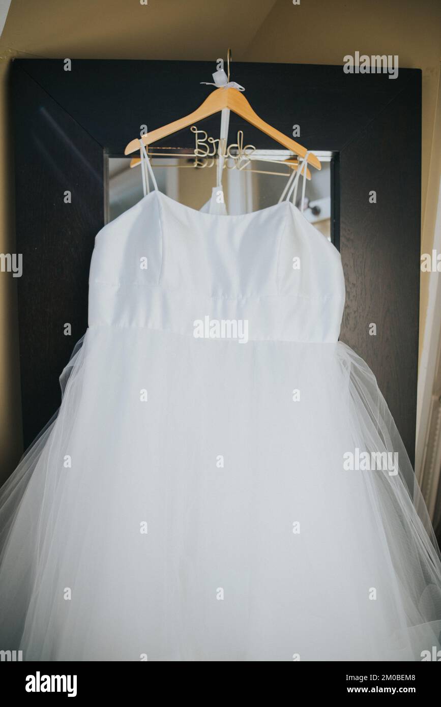 A vertical of the bride's white dress hanging off a hanger in front of ...