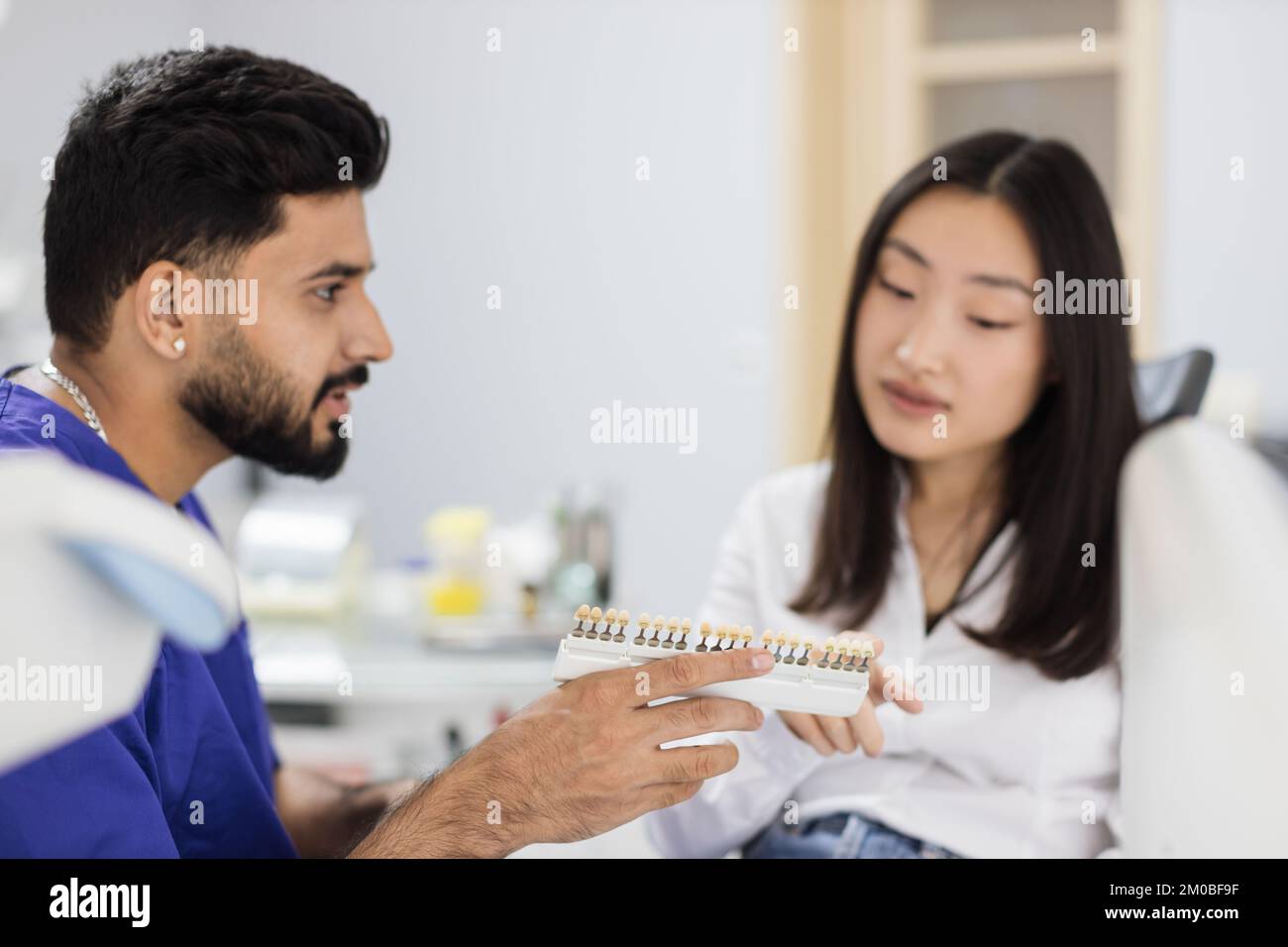 Attractive male dentist checking and selecting color of young asian ...