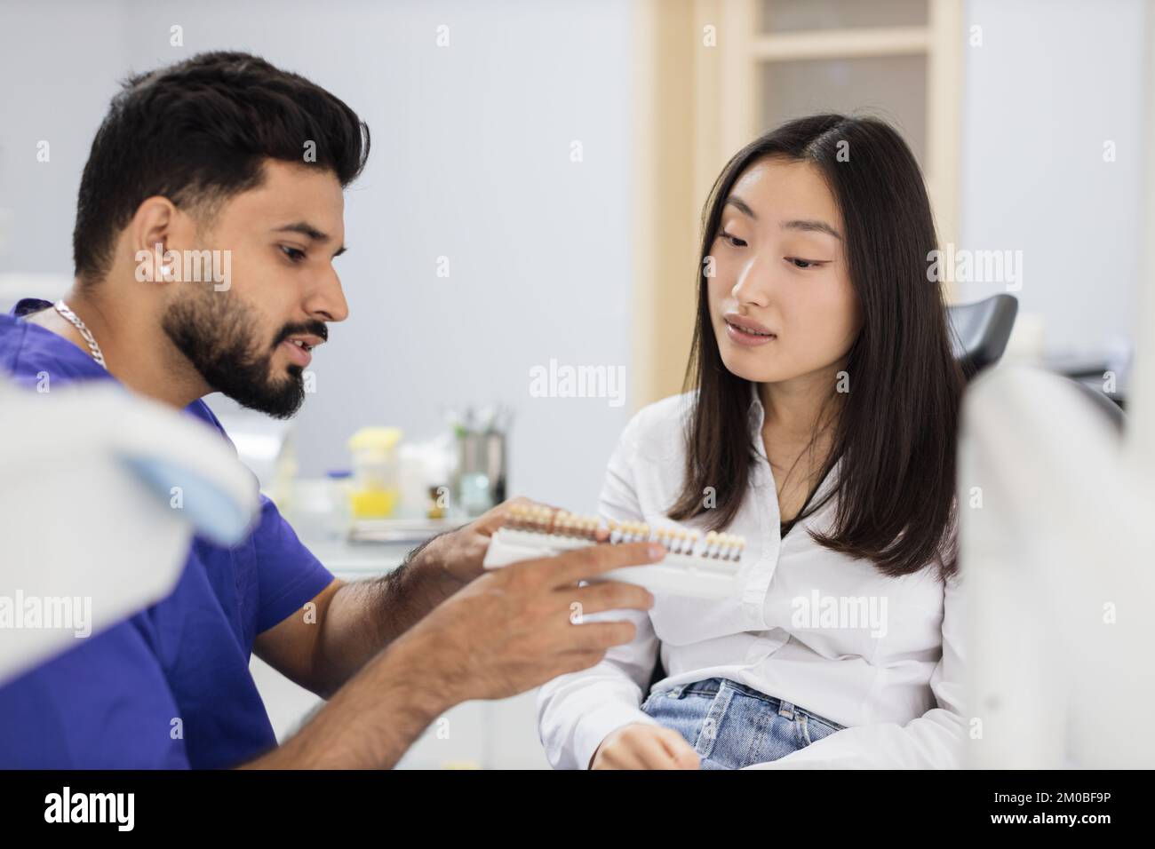 Attractive male dentist checking and selecting color of young asian ...