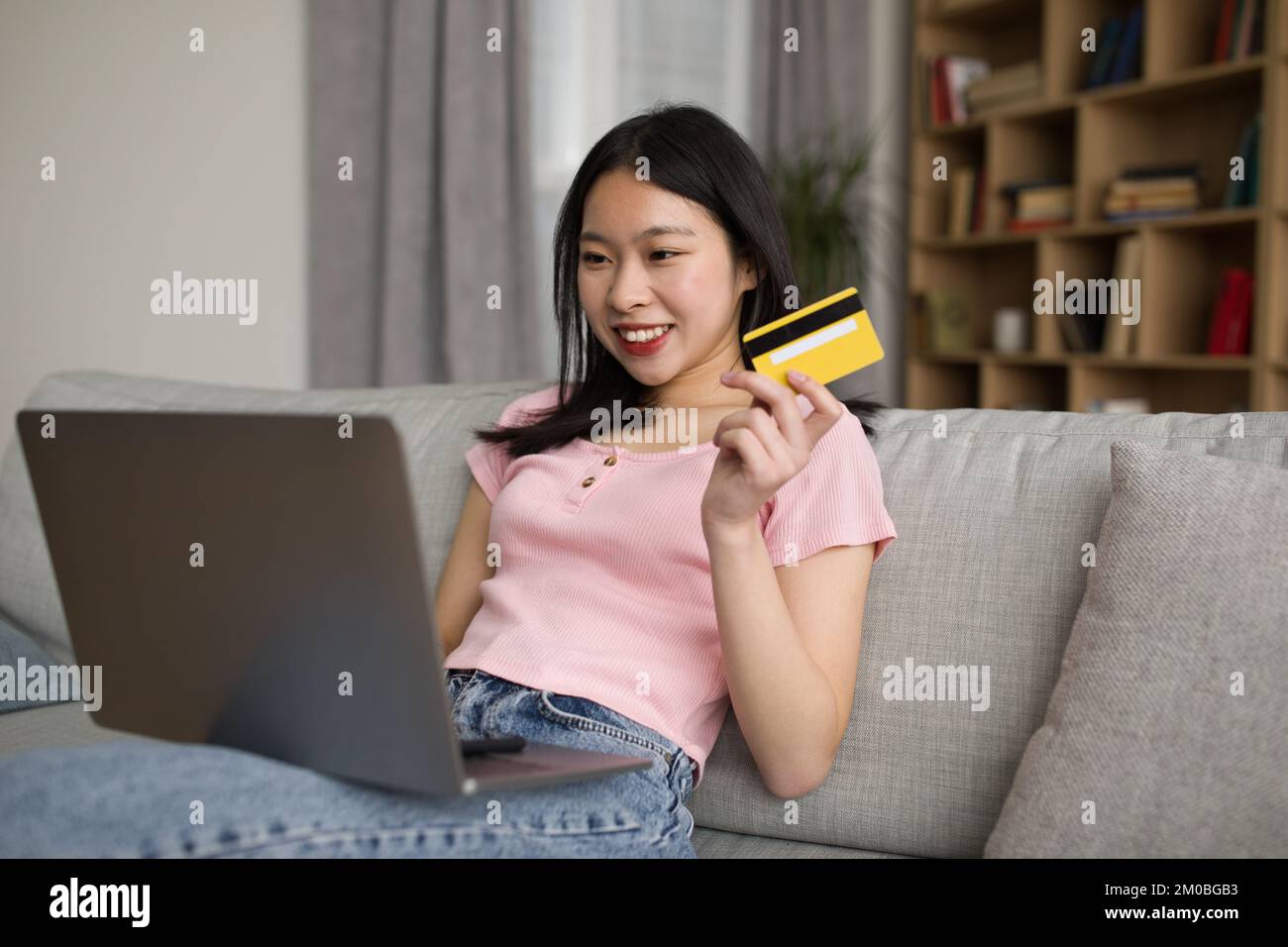 Positive asian lady holding credit card and using laptop, shopping ...