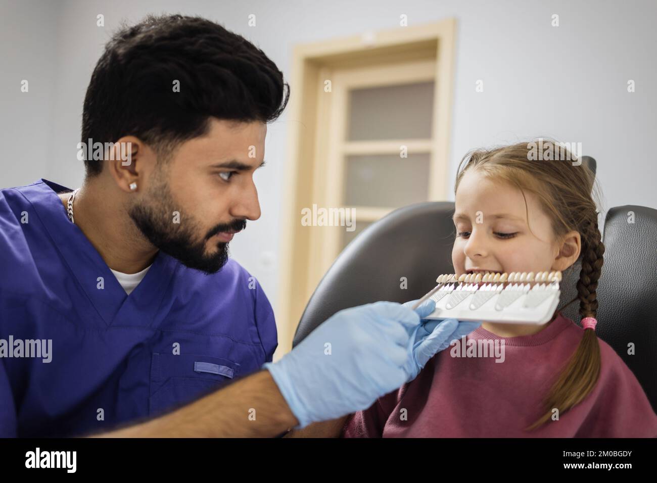 Confident dentist checking and selecting color of young caucasian girl ...