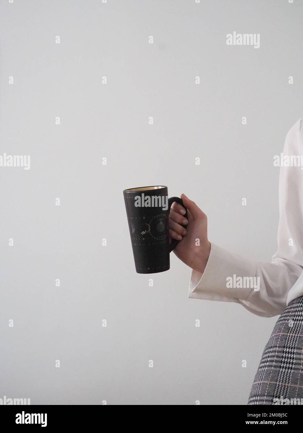 A vertical shot of a woman's hand holding a coffee mug on a grey ...