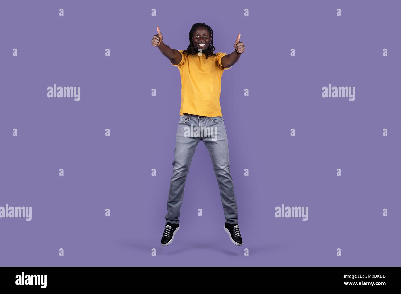 Happy black man showing thumb ups while jumping on purple Stock Photo ...