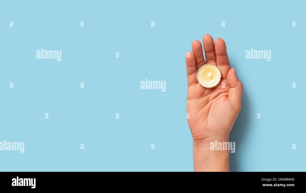 Tea light candle in the hand palm over blue background. Scented round ...